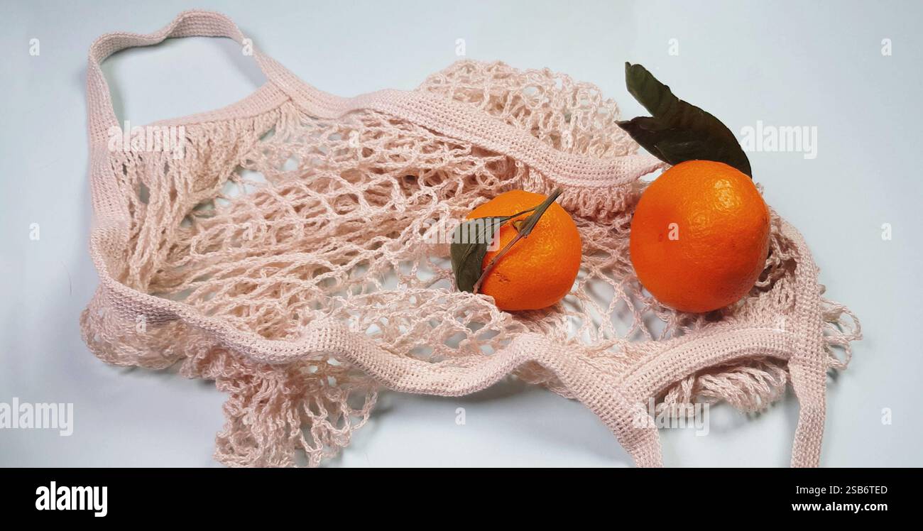Tangerines with green leaves are placed in a white reusable food mesh ...