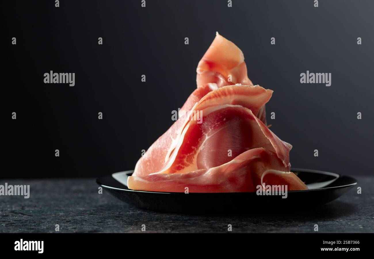 Italian prosciutto crudo, raw ham leg sliced on a black plate Stock ...