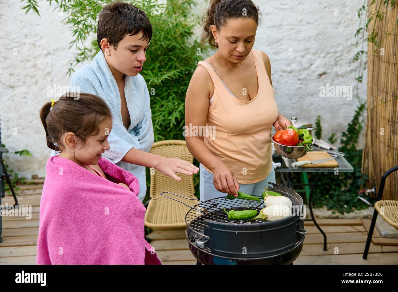 A family gathers around a barbecue grill in their backyard, cooking ...