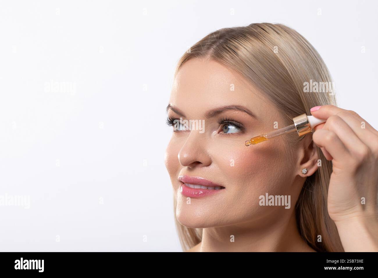 A woman is carefully applying a serum to her face, enhancing her ...