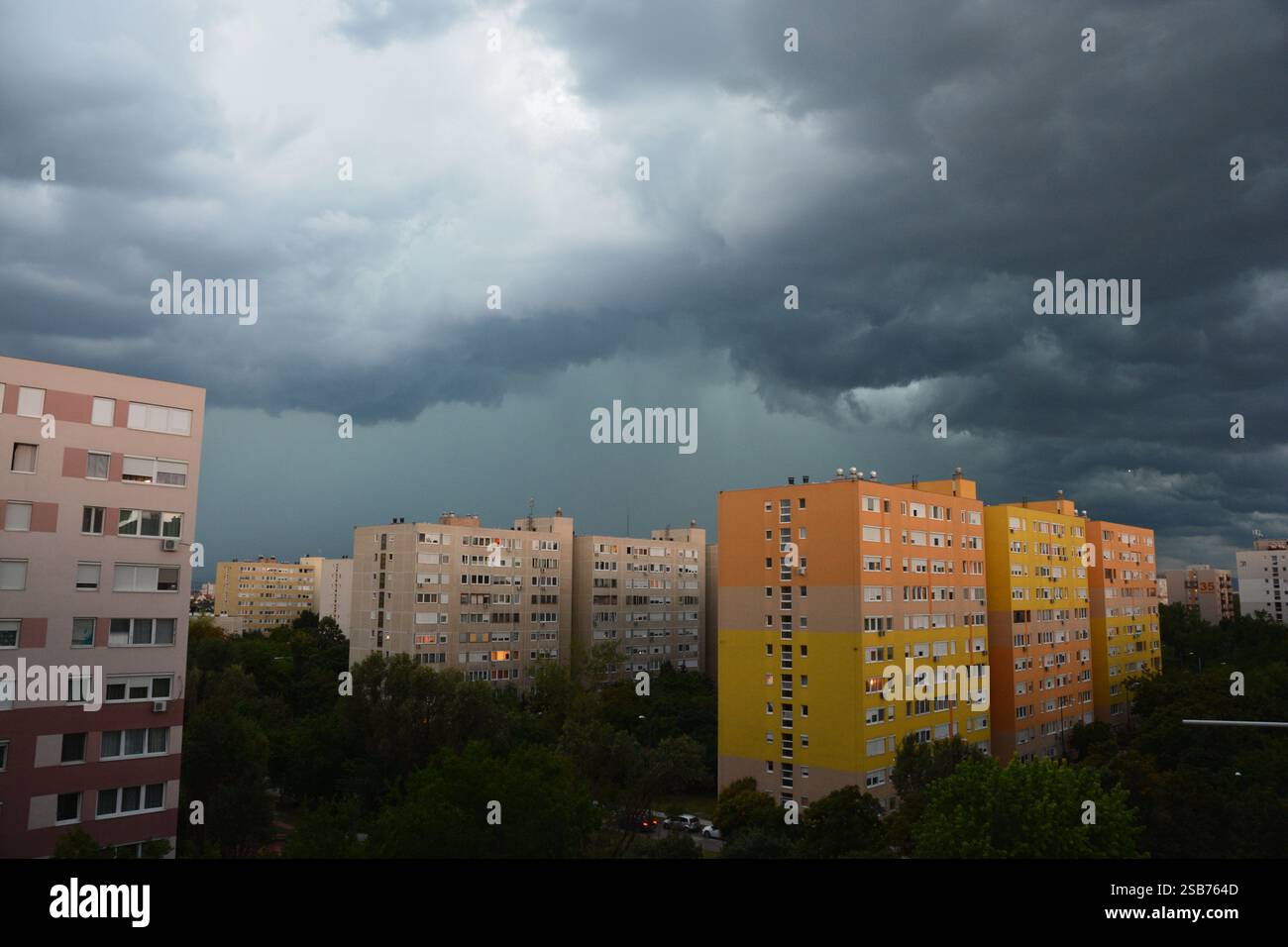 A dramatic view of a Budapest housing estate through a window, with dark black clouds on the ...