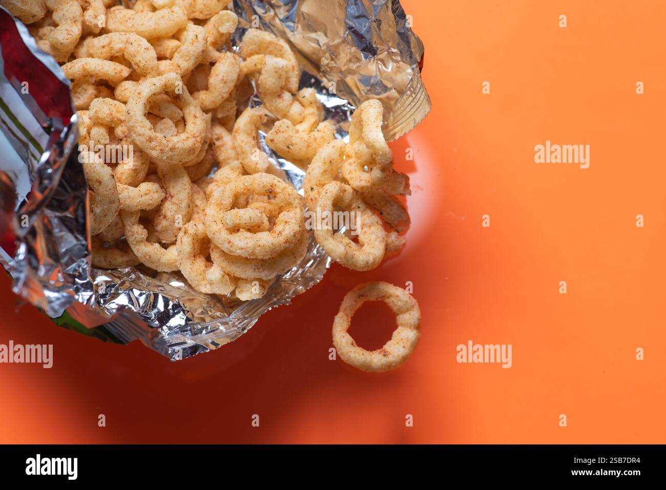 Curled snacks spilling from a shiny packet against a striking orange ...