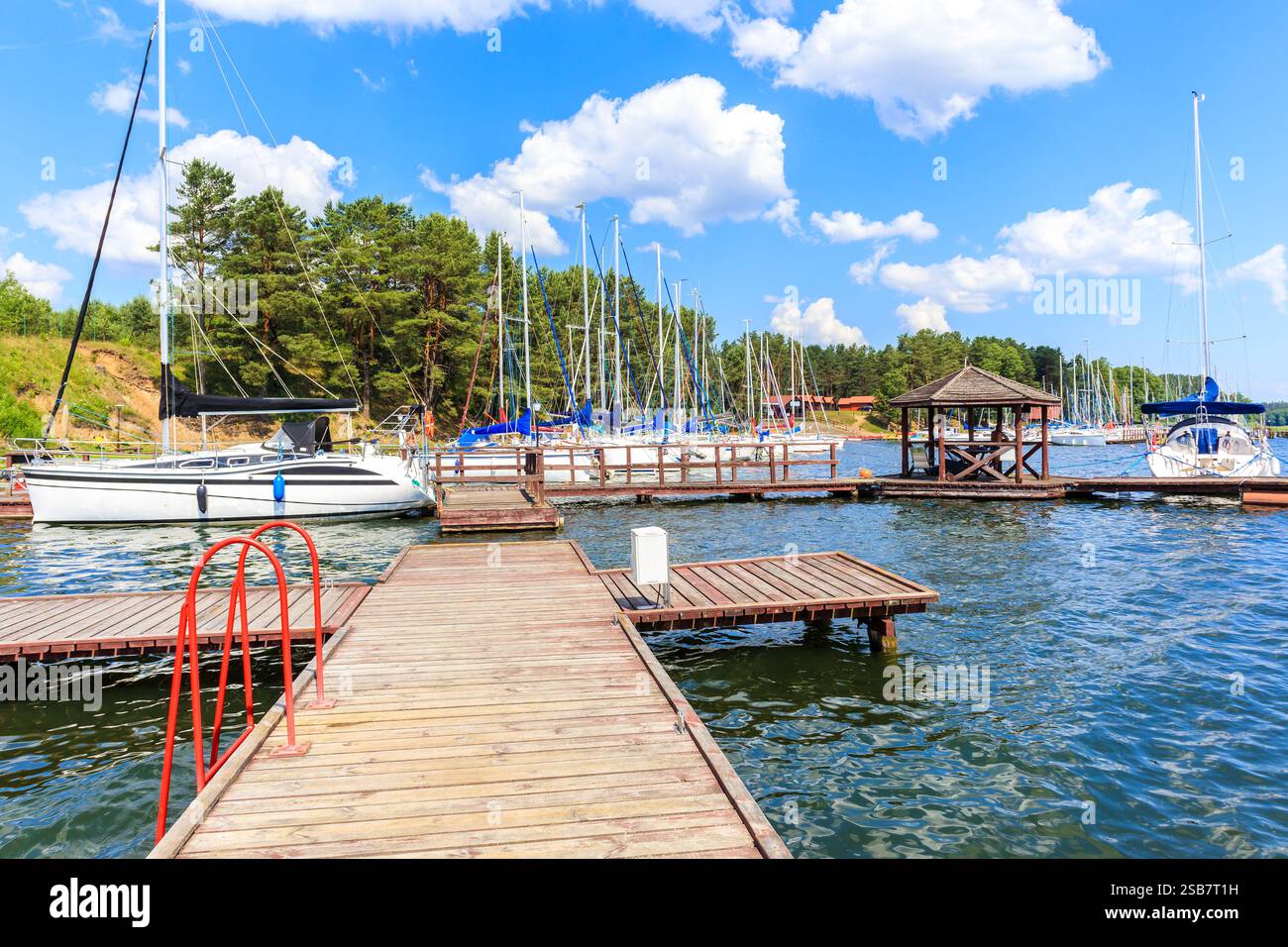 Sailing boats and pier on lake shore in Krzyze village port on sunny ...
