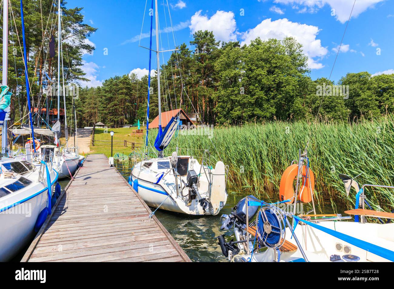 Sailing boats and pier on lake shore in Krzyze village port on sunny ...