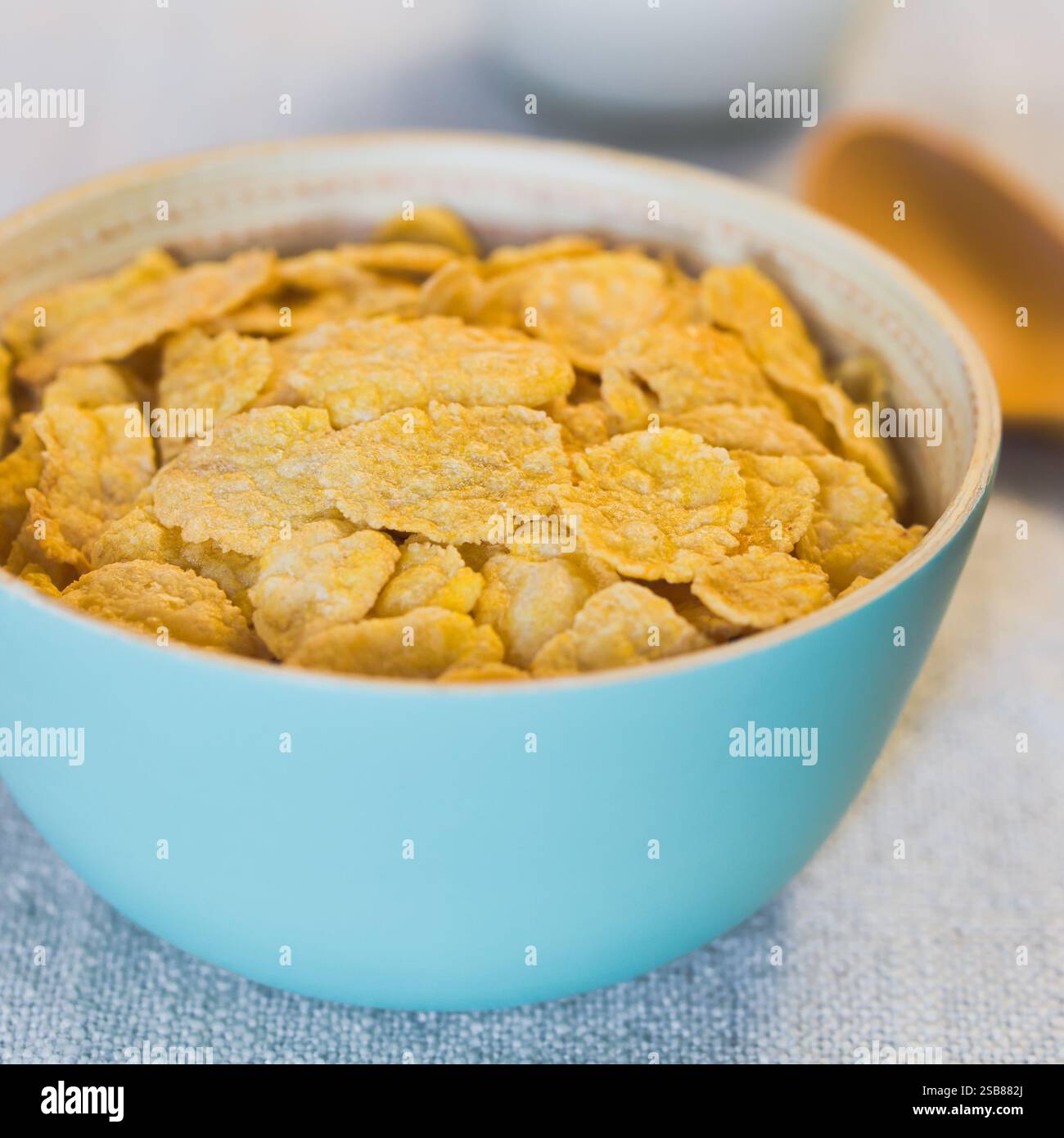 Crispy unsweetened corn flakes in blue bowl, milk and spoon in the back ...