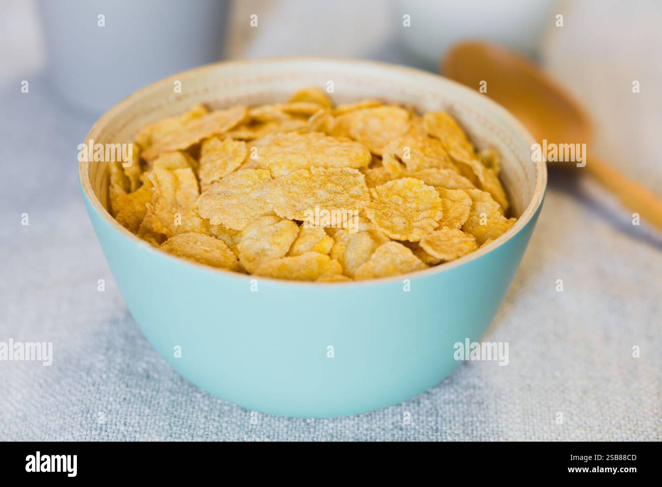Crispy unsweetened corn flakes in blue bowl, milk, cup and spoon in the ...