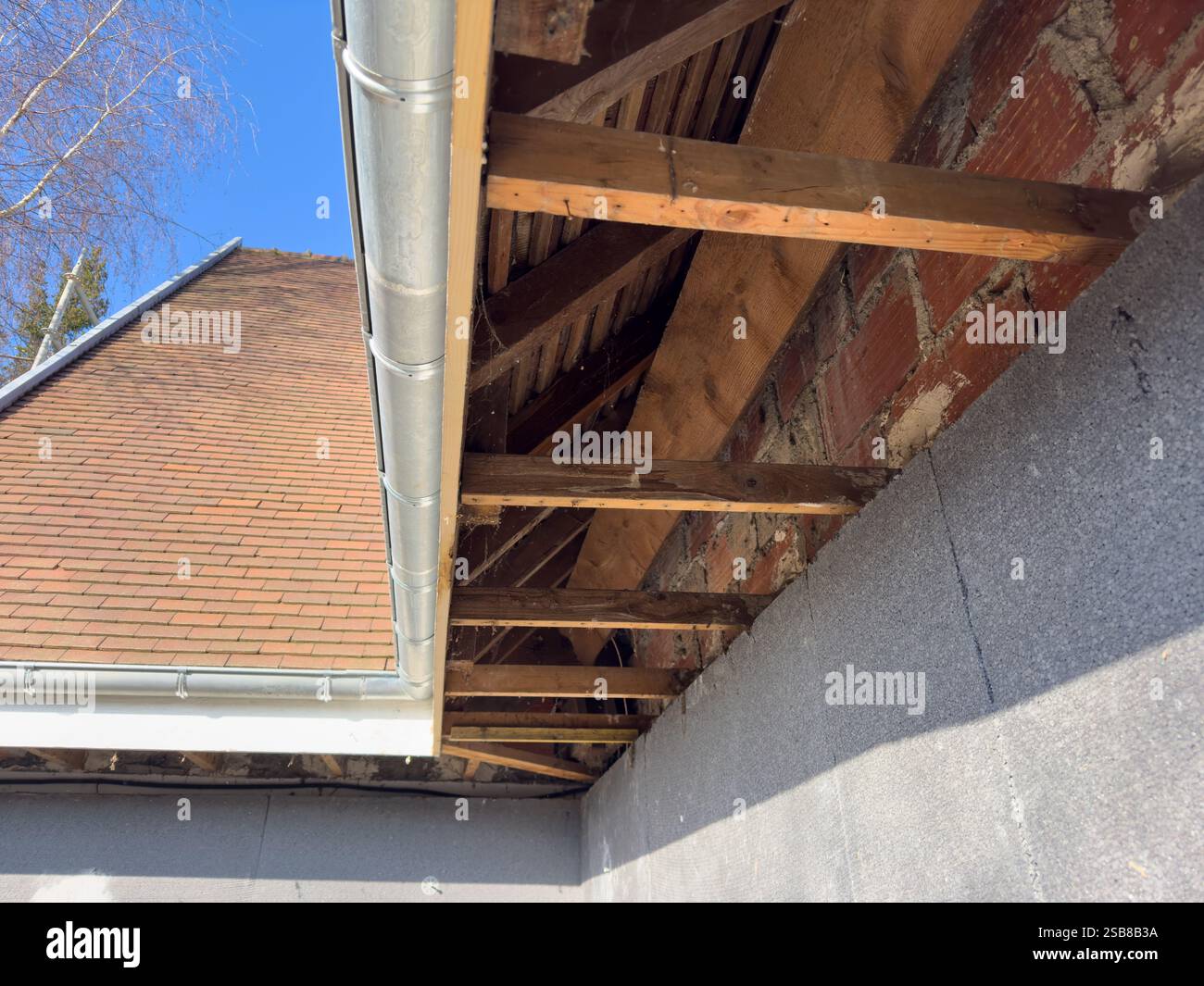 Roof renovation reveals wooden beams in a rustic home under clear blue ...