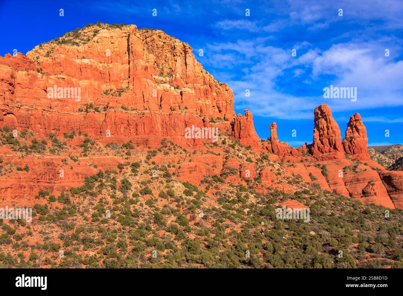A mountain with a red rock face and a blue sky. The mountain is covered ...