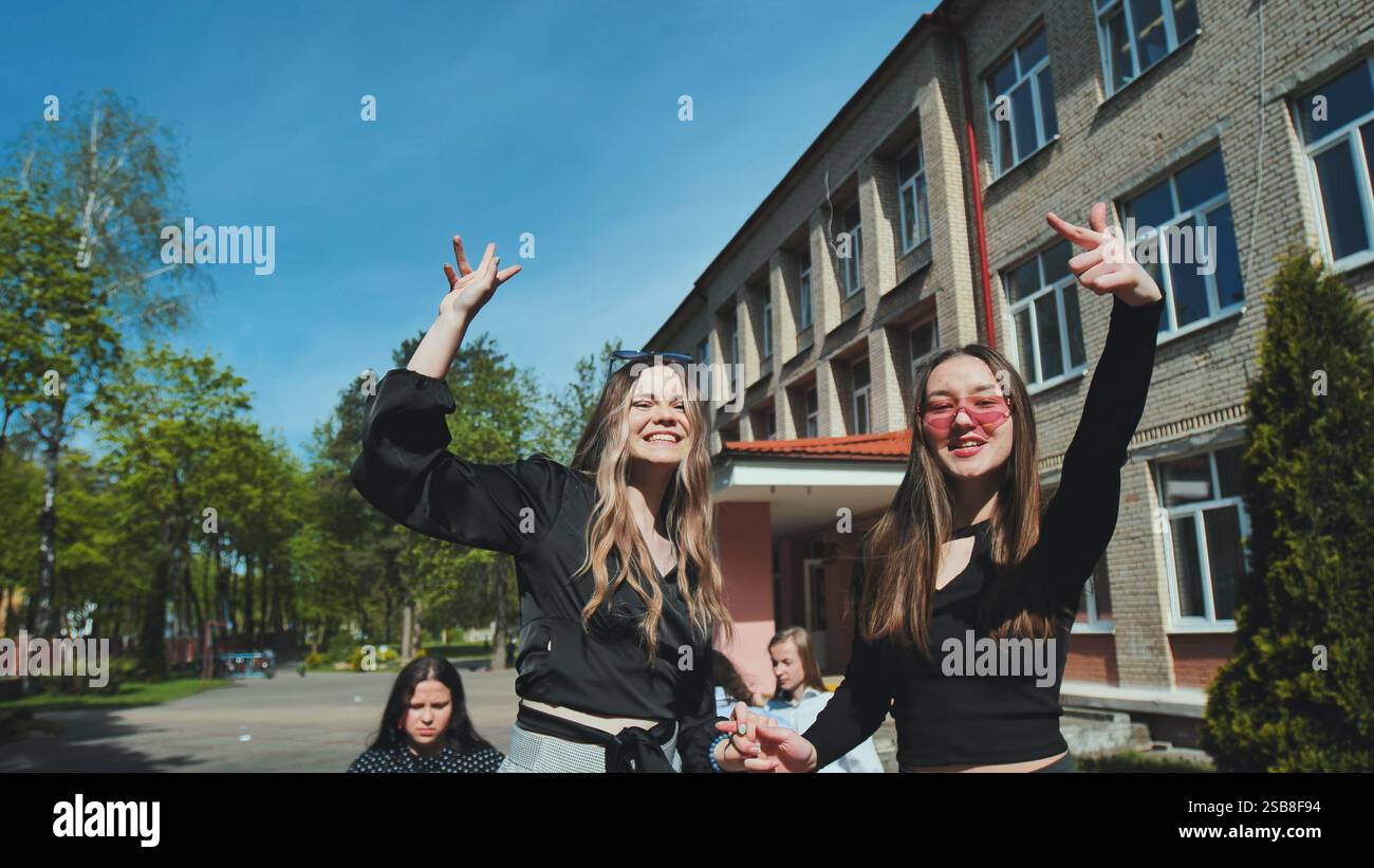Two happy students gesturing and smiling in front of their high school ...