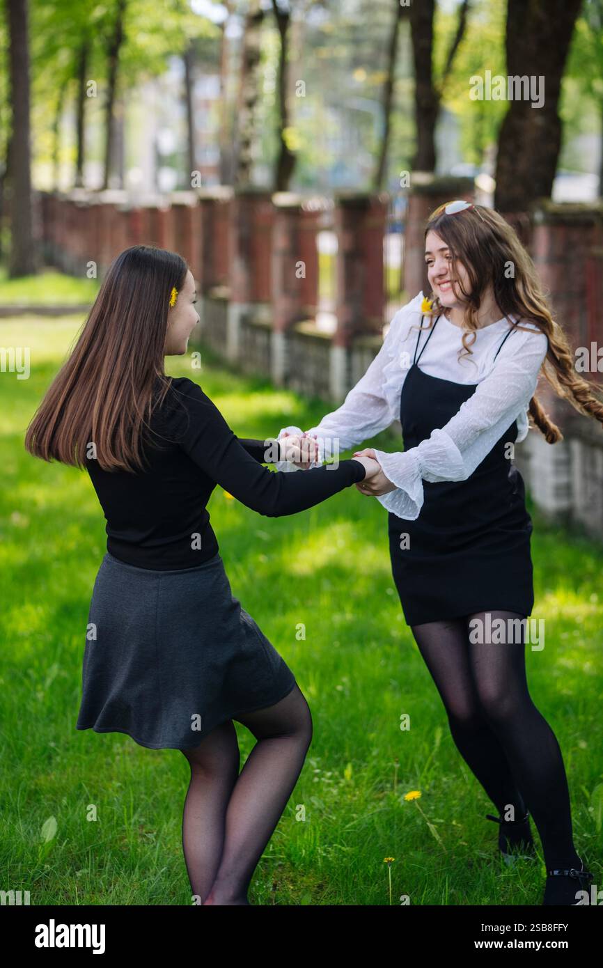 Two joyful schoolgirls in matching black and white outfits twirling ...