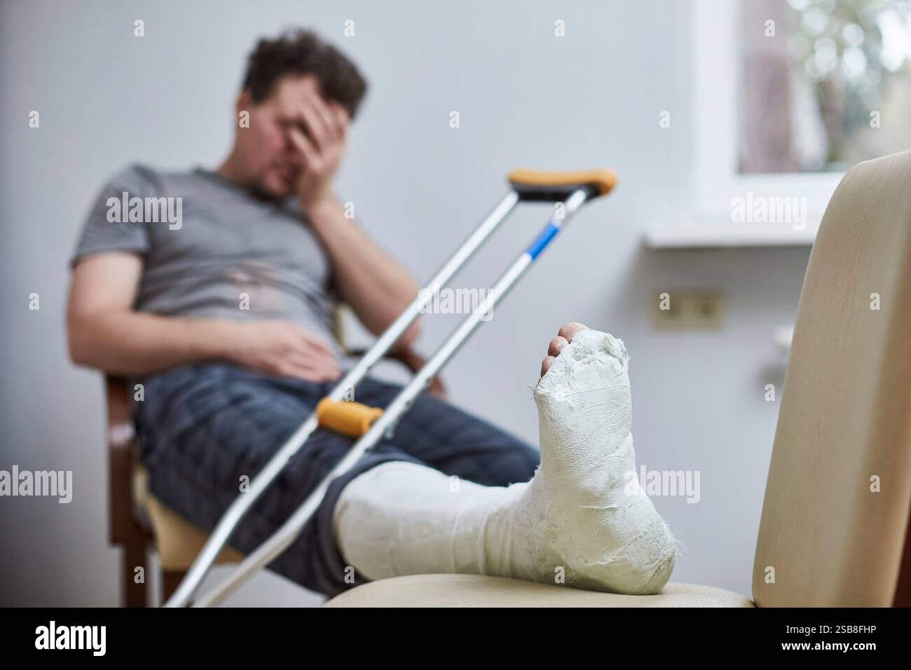 A sad man with a broken leg sits on a chair. Illness concept Stock ...