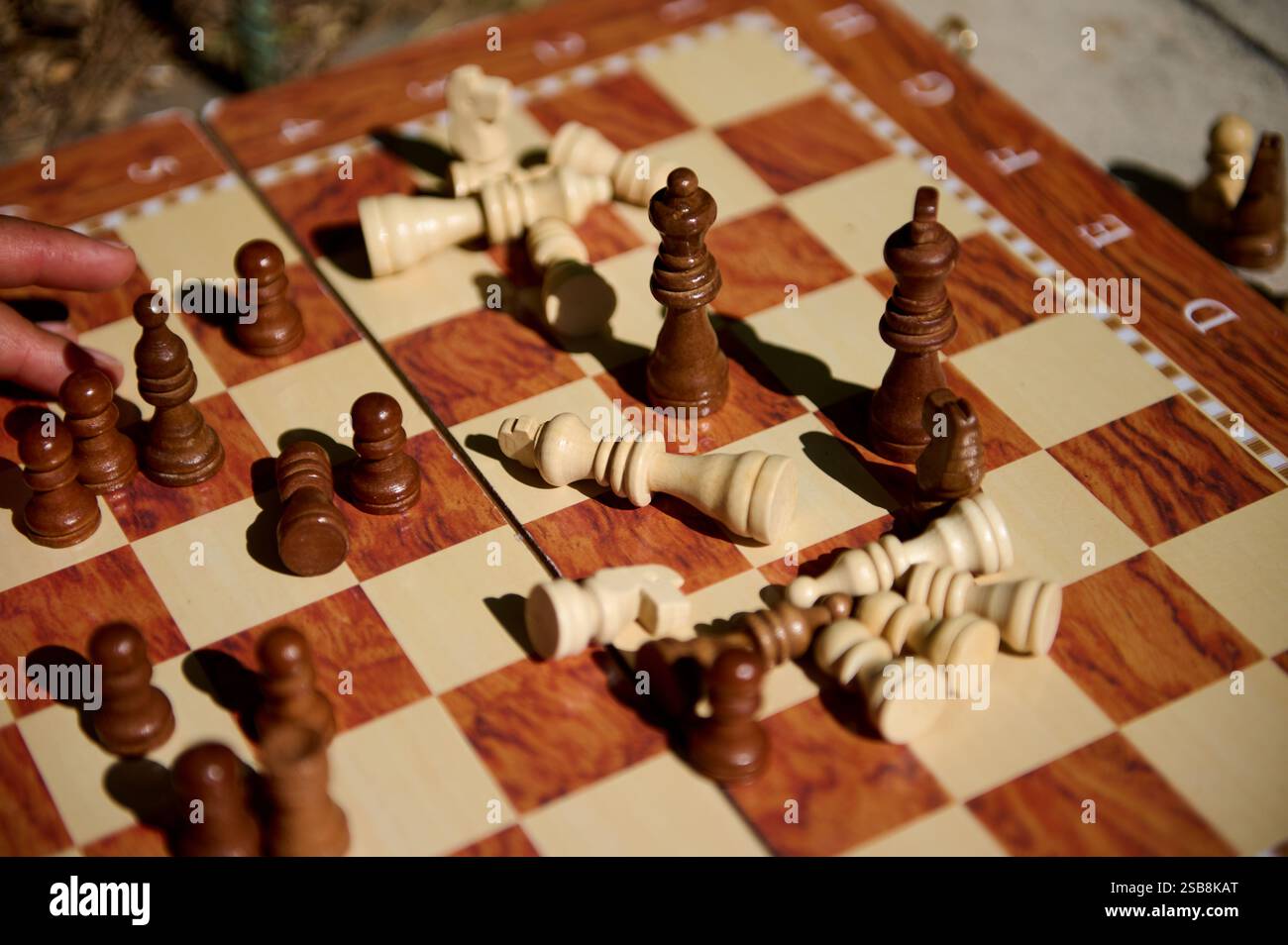 A wooden chessboard displays scattered chess pieces, showcasing the ...