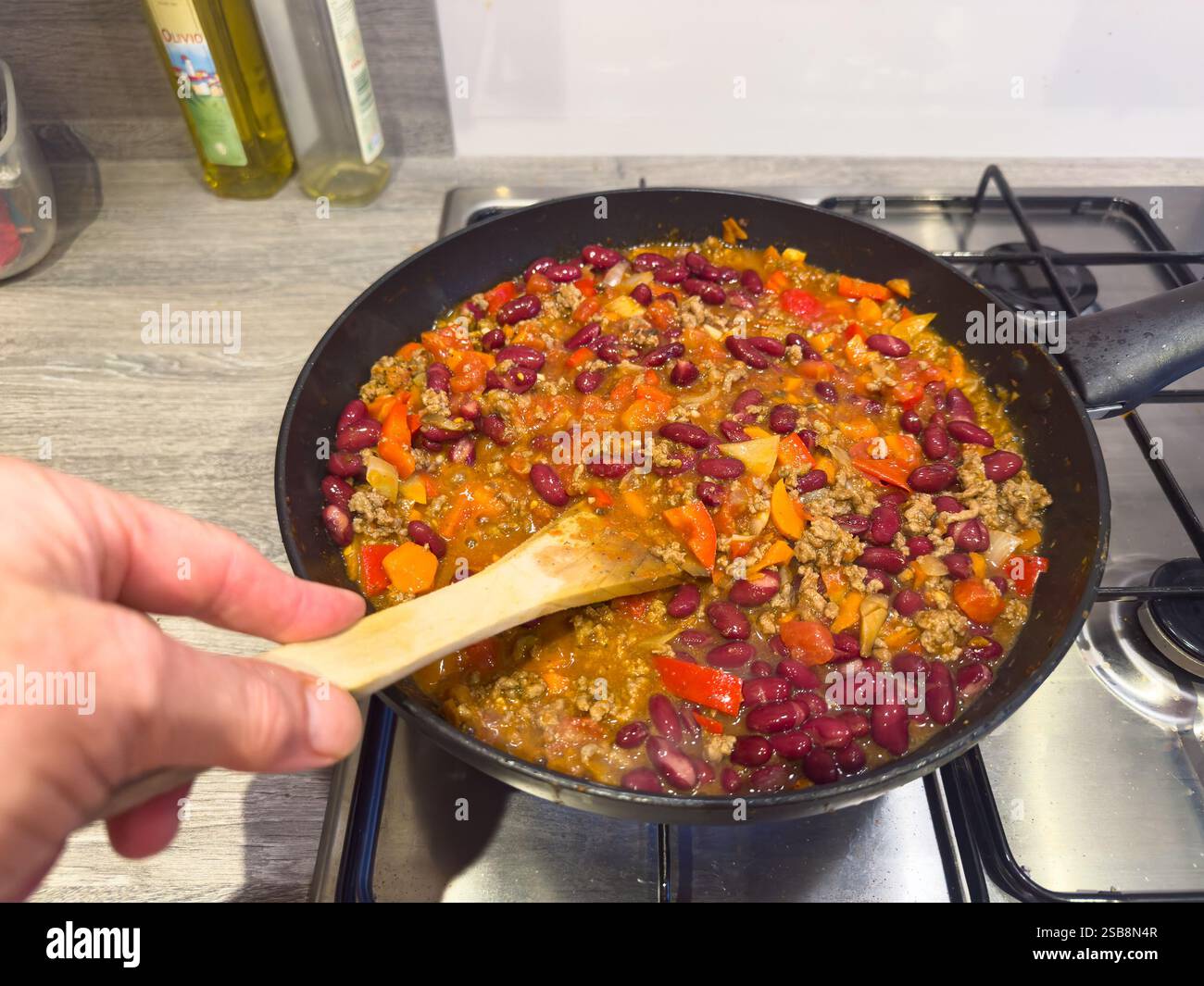 large wok and man cooking and stirring a minced beef chilli con carne ...