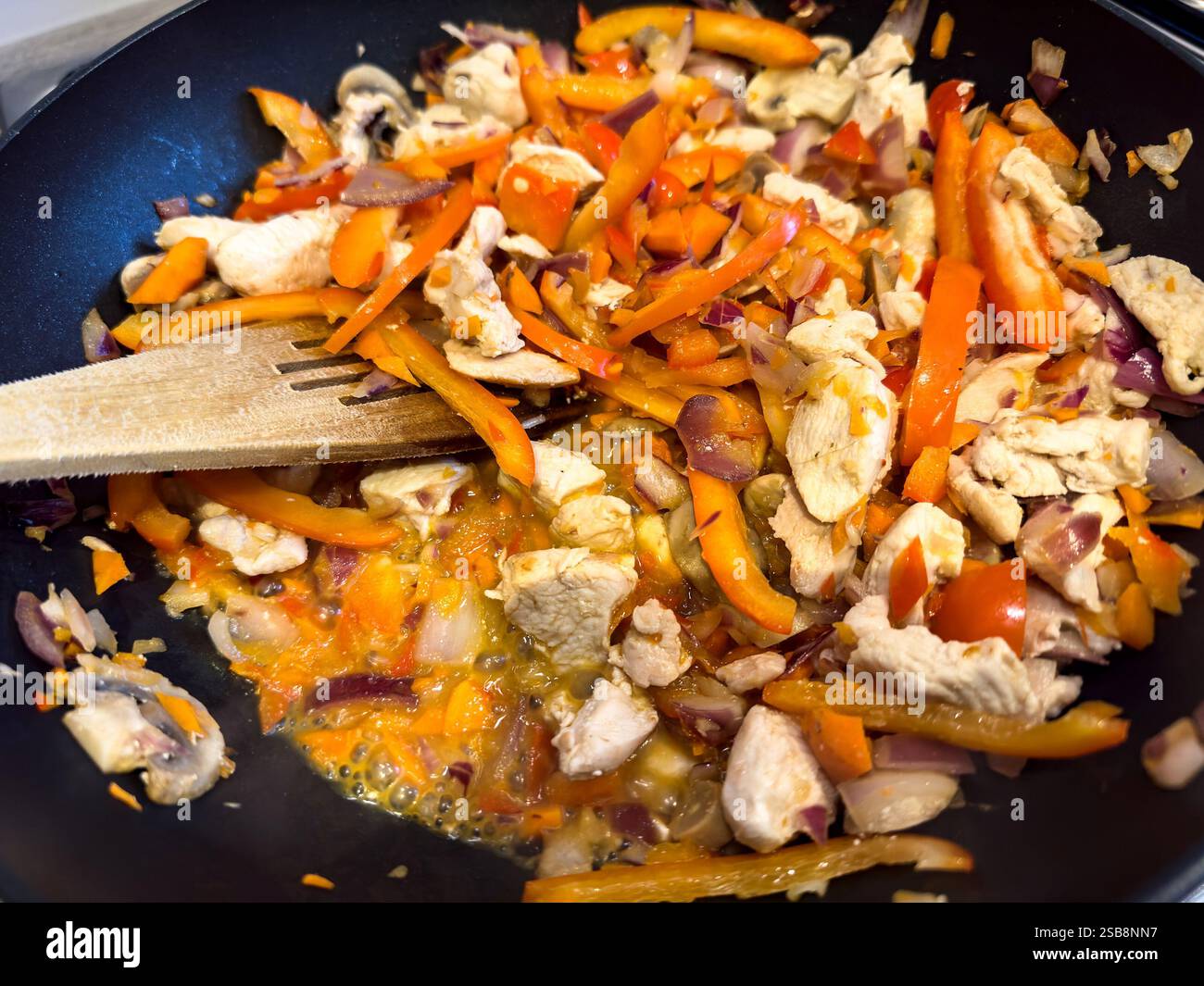 large wok cooking and stirring a chicken curry with peppers & mushrooms ...