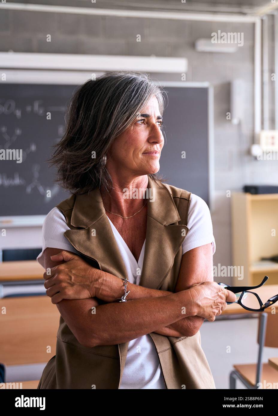 A teacher stands alone in an empty classroom, gazing thoughtfully out ...
