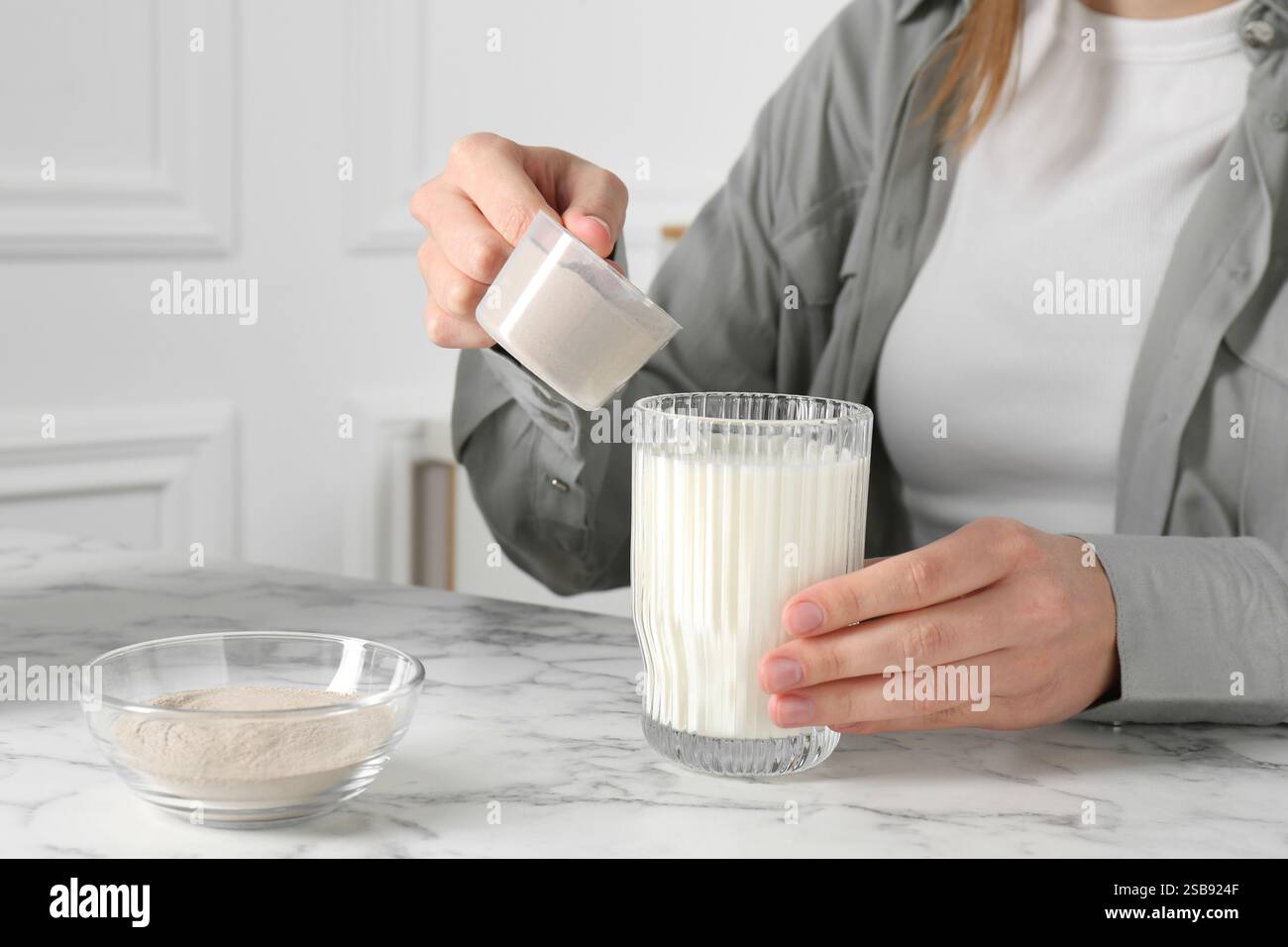 Making protein cocktail. Woman adding powder into glass with milk at ...