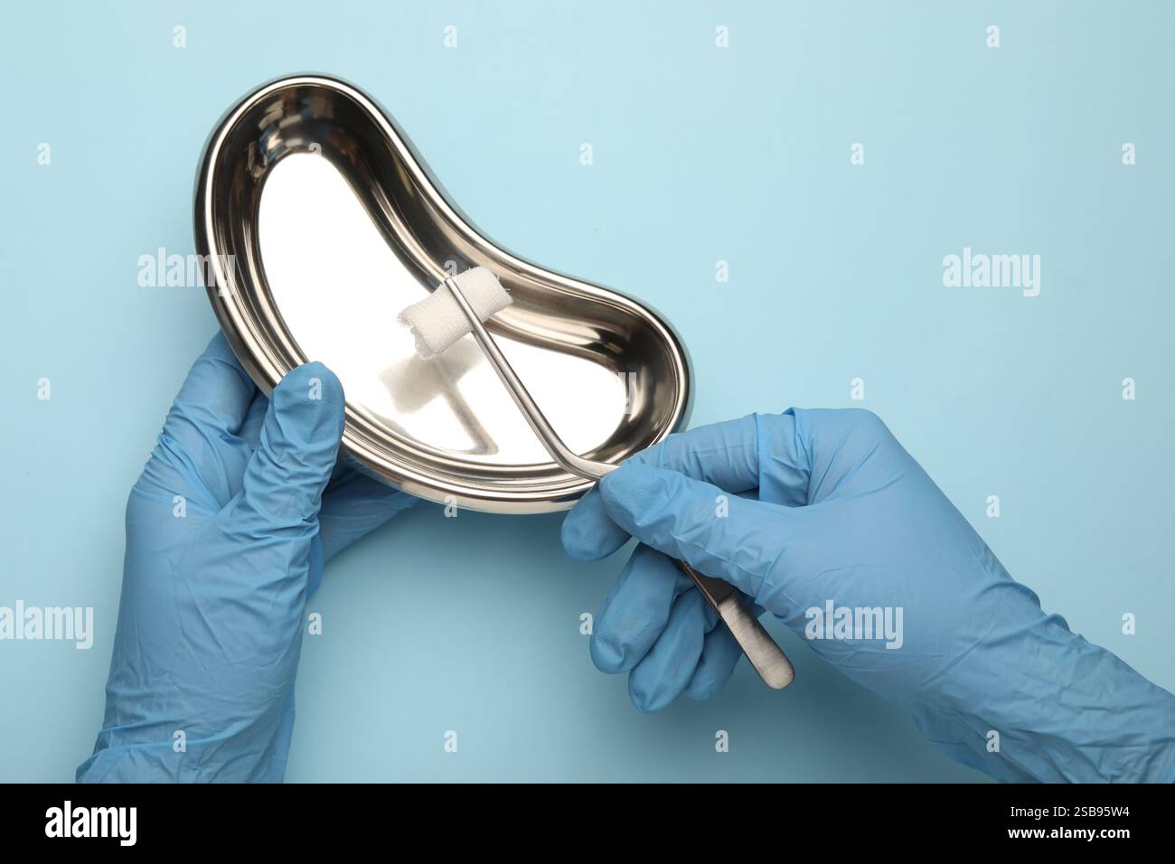 Doctor holding surgical tweezers with gauze and tray on light blue ...