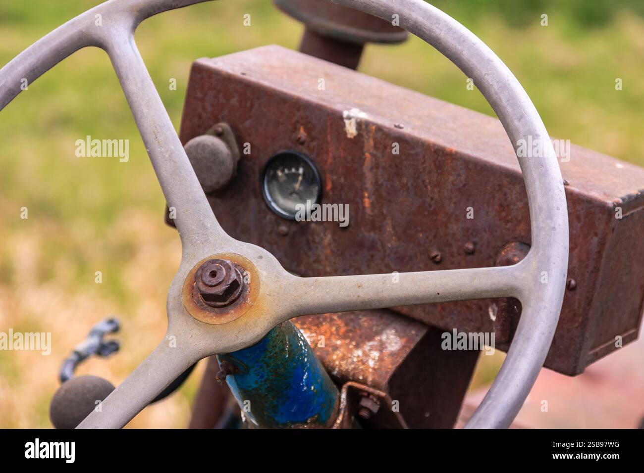 A rusted old tractor steering wheel with a gauge on the front. The ...