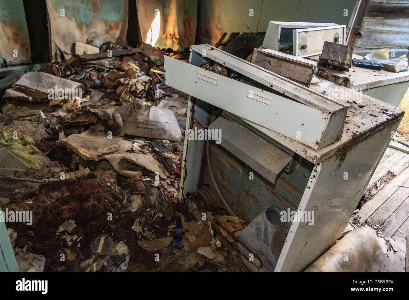 A dirty, broken, and rusted old oven sits in a room full of trash. The ...
