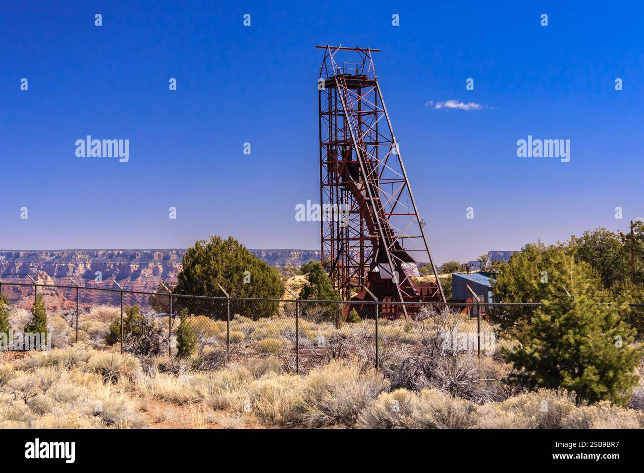 A rusty old tower stands in a field with a blue sky in the background ...