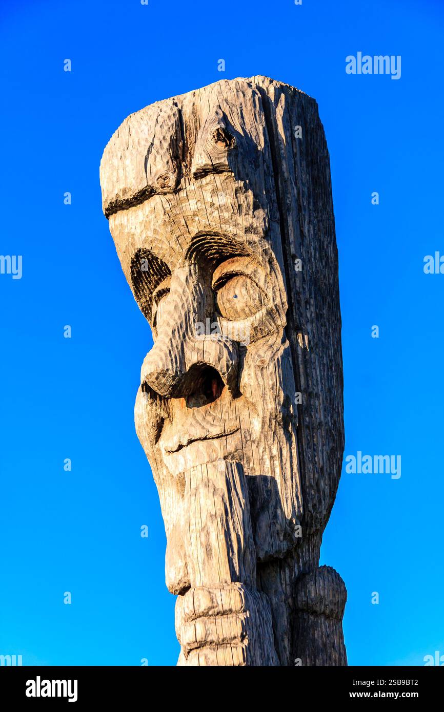 A wooden statue of a face is standing in front of a blue sky. The ...