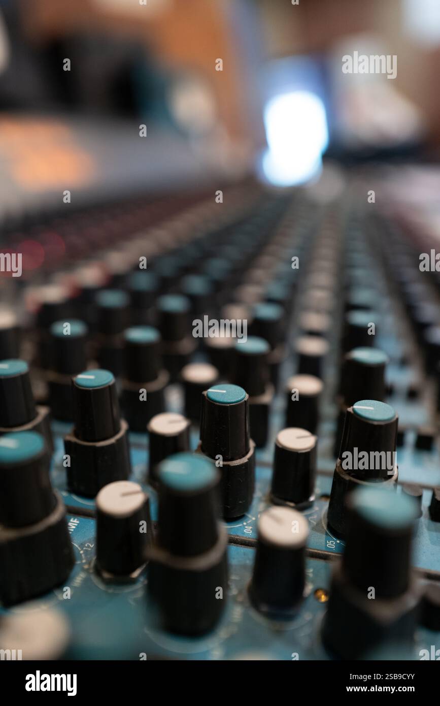 A detailed view showcases a sound mixing console filled with black and teal knobs arranged ...