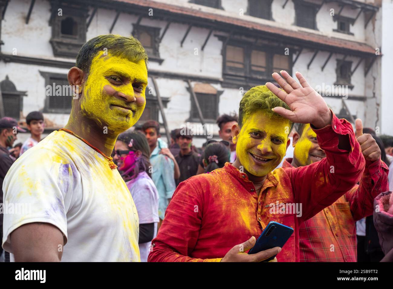 Two smiling Nepali men waving with their faces covered in yellow during ...