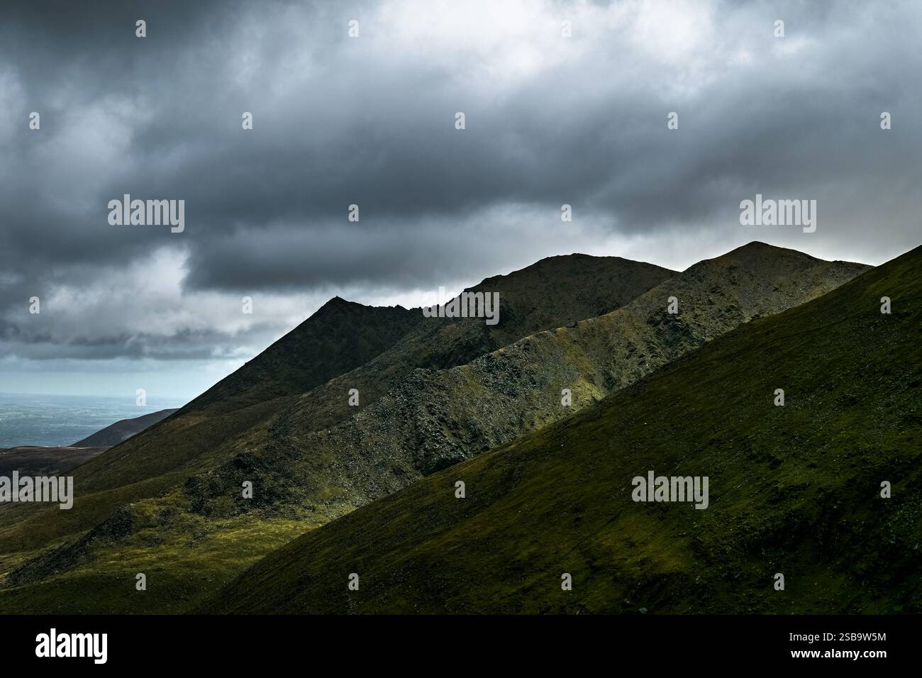 Sharp mountain peaks against a dark, stormy sky, lower slopes in shadow ...