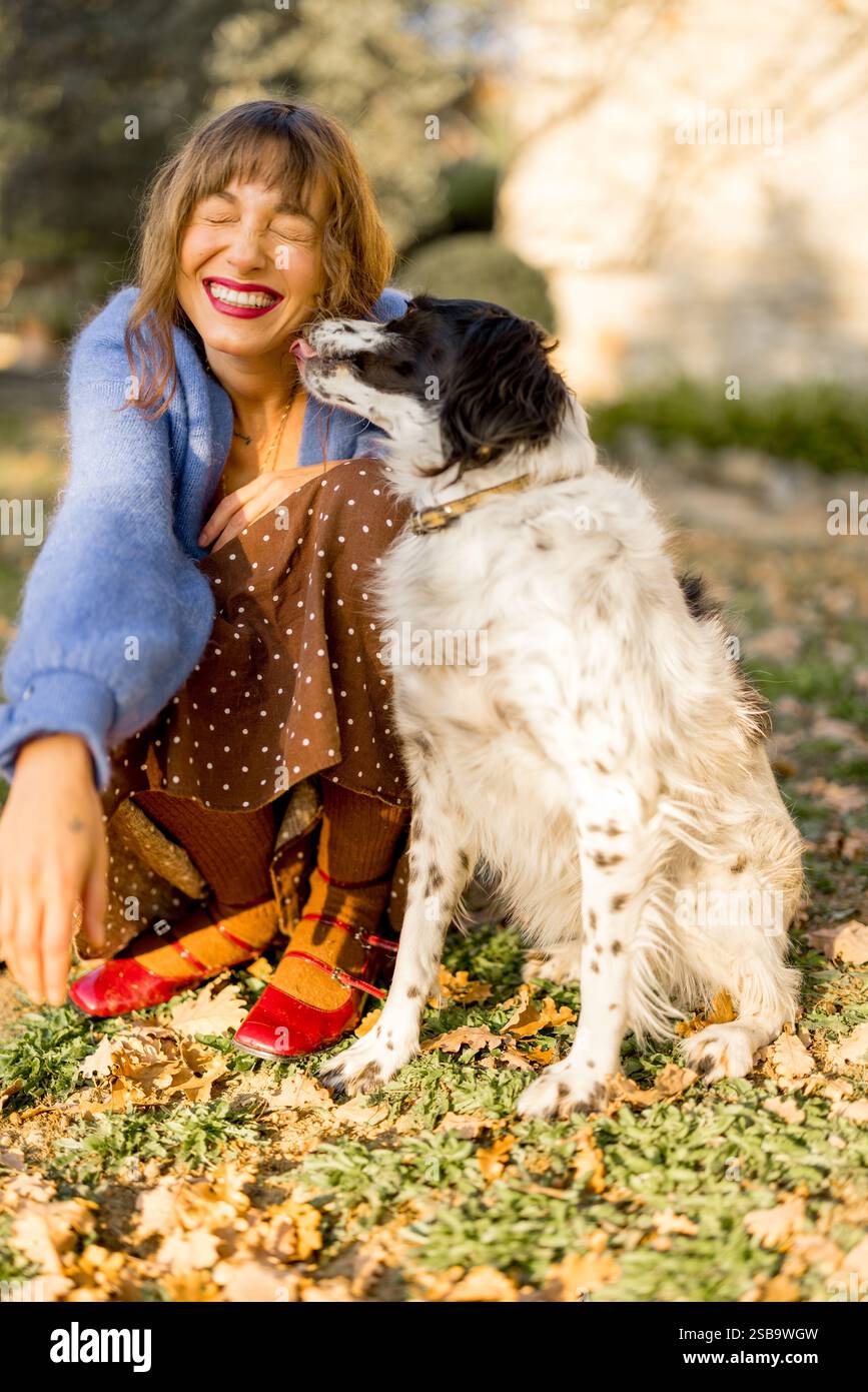 A cheerful woman with two dogs sitting in a sunny countryside setting ...