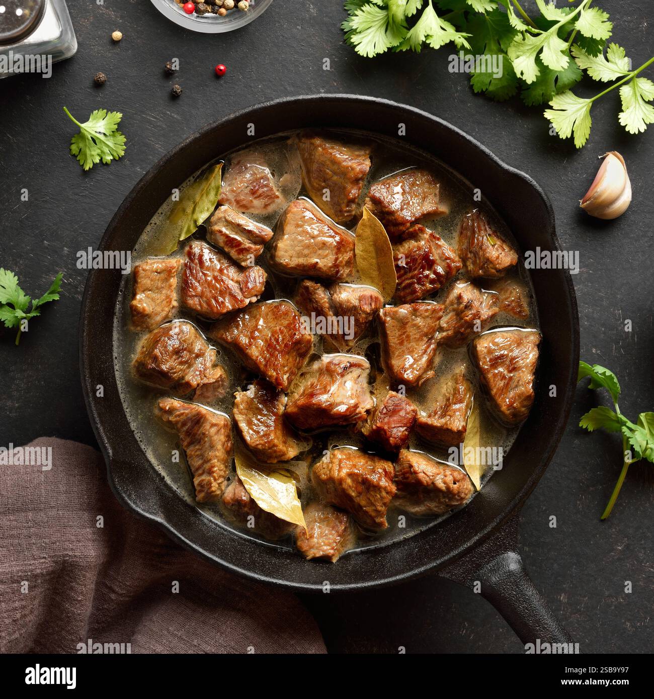 Braised beef in cast iron skillet over dark stone background. Beef ...