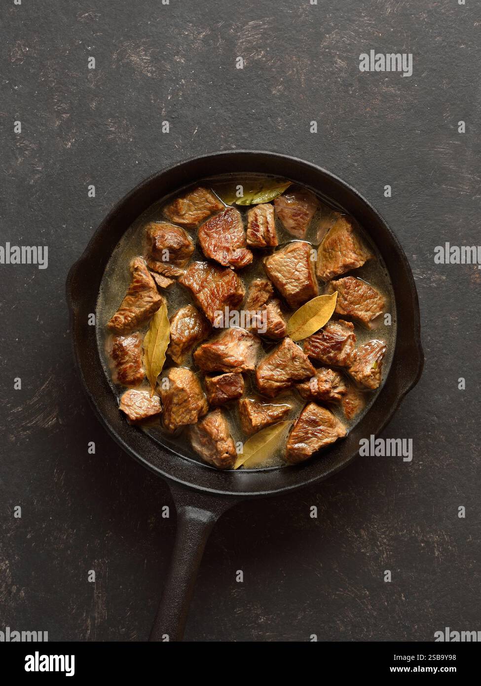 Braised beef in cast iron skillet over dark stone background. Beef ...