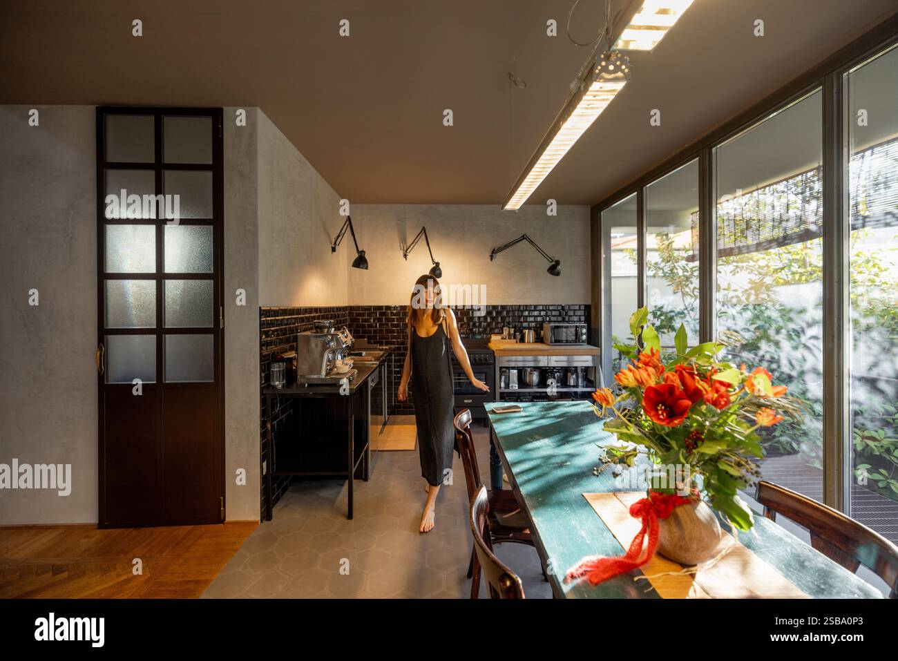 A barefoot woman walks through a stylish kitchen with dark tiles ...