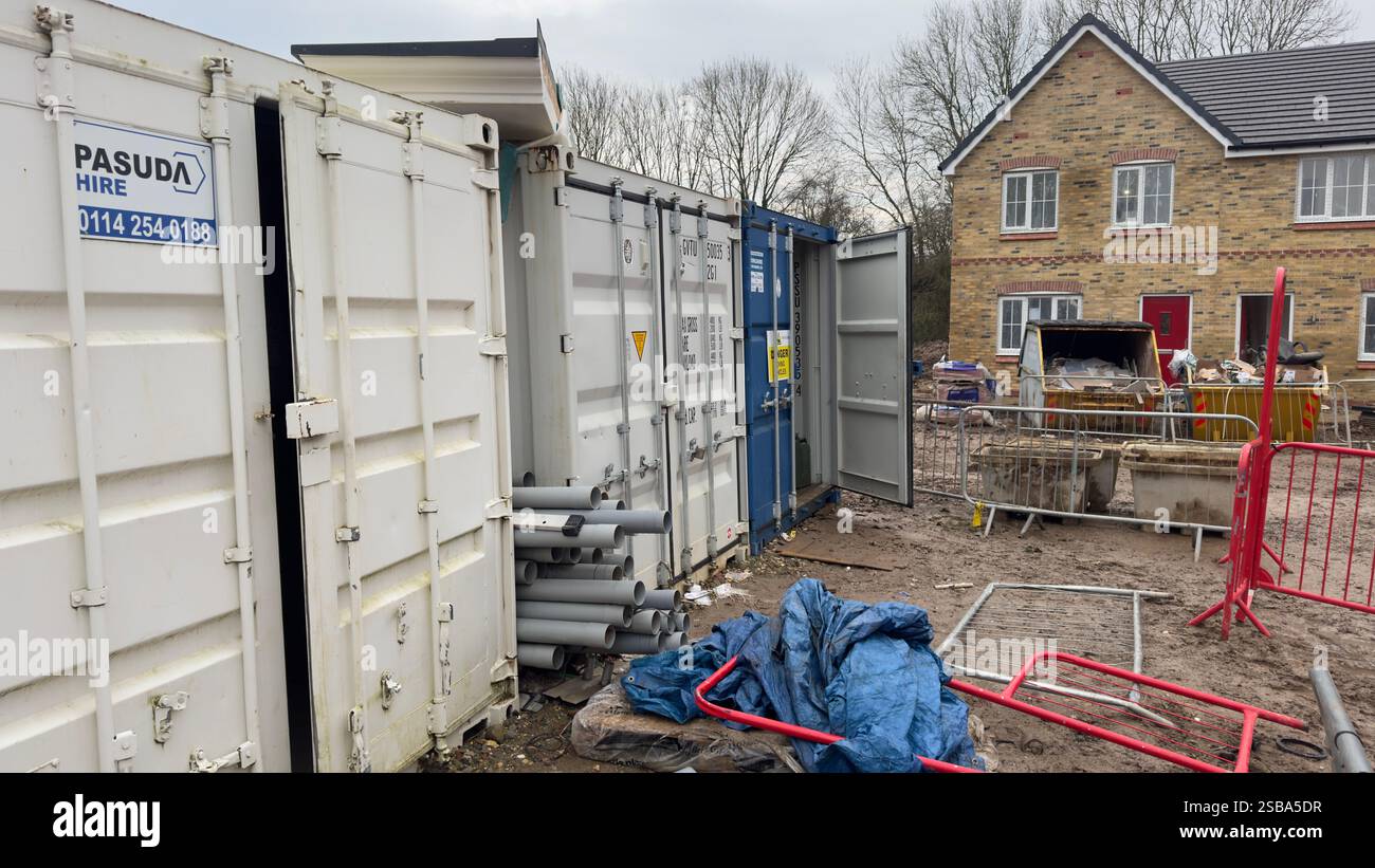 Construction site with shipping containers, building materials, and a partially completed house ...