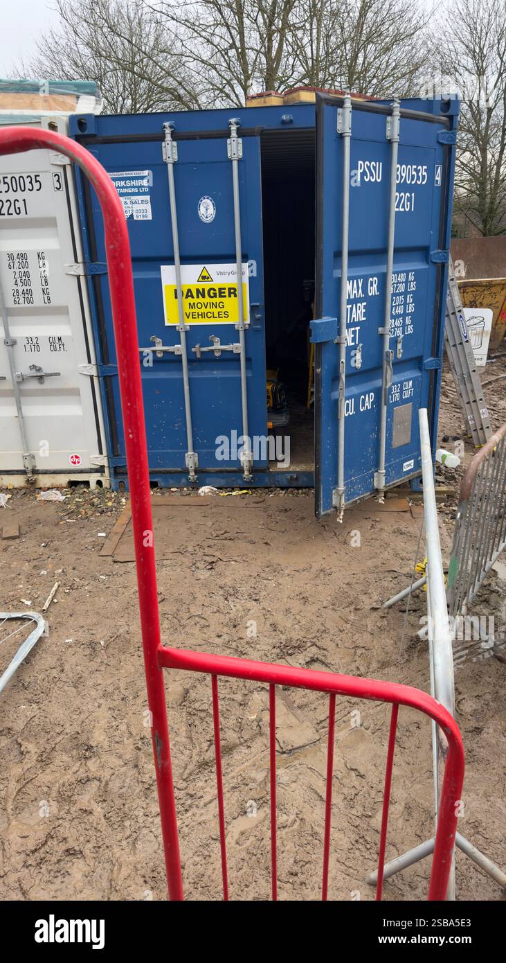 A blue shipping container, partially open, sits on muddy ground near a ...