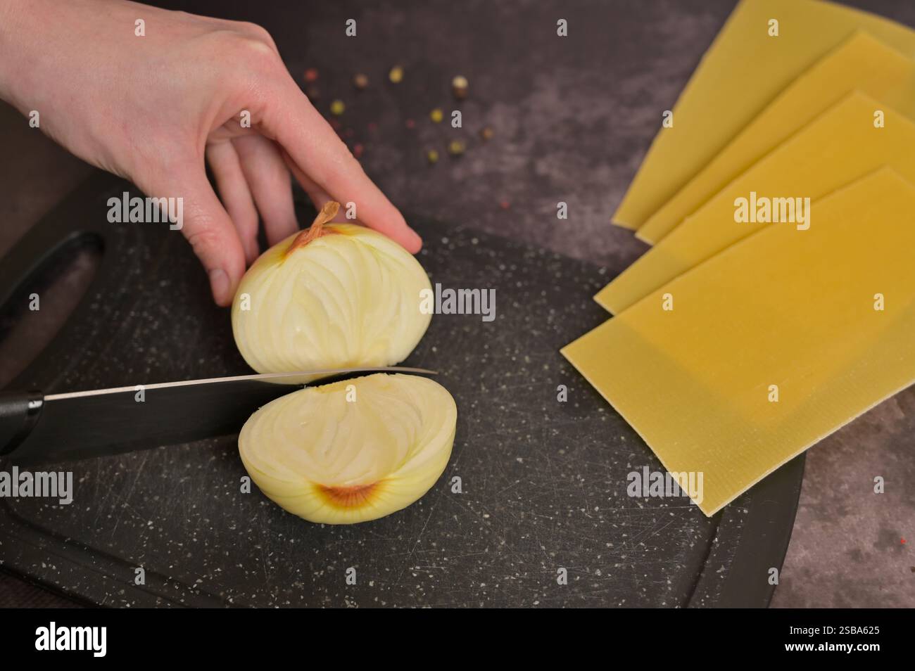 Woman's hand cutting onion in half on the black kitchen cutting board ...