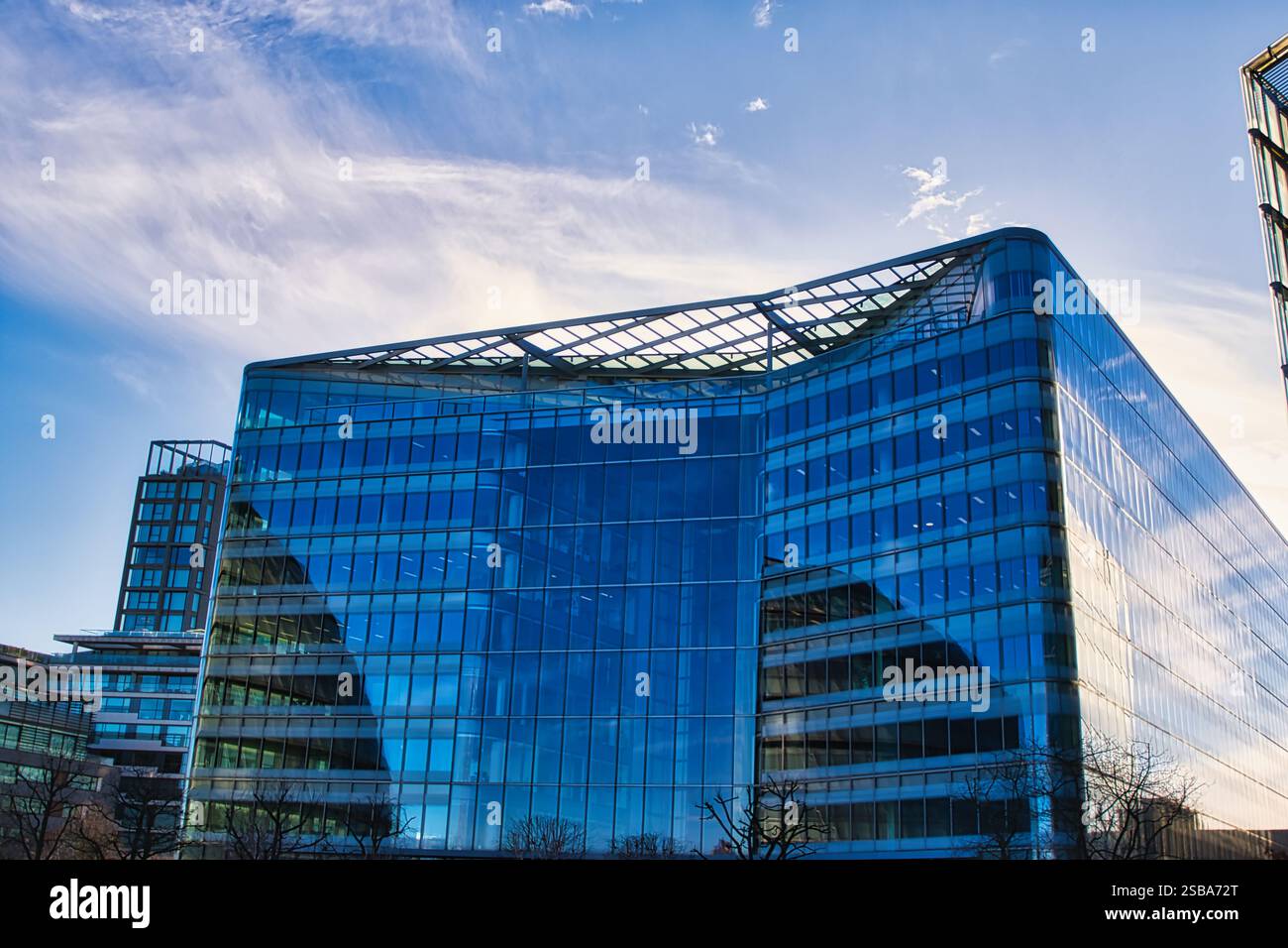 A modern glass-fronted building dominates the image, reflecting a blue ...