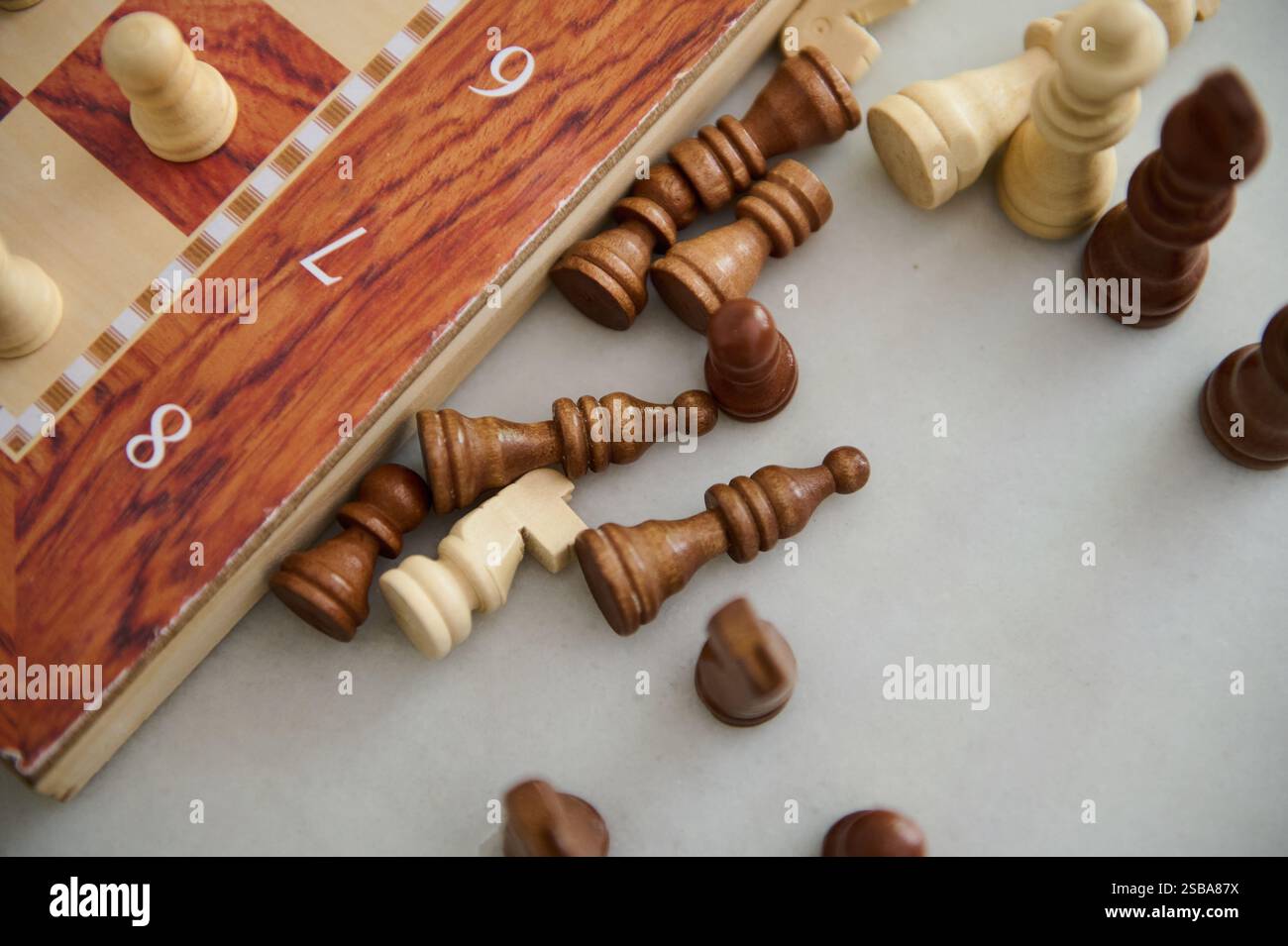 A chessboard with wooden-colored squares and scattered chess pieces ...