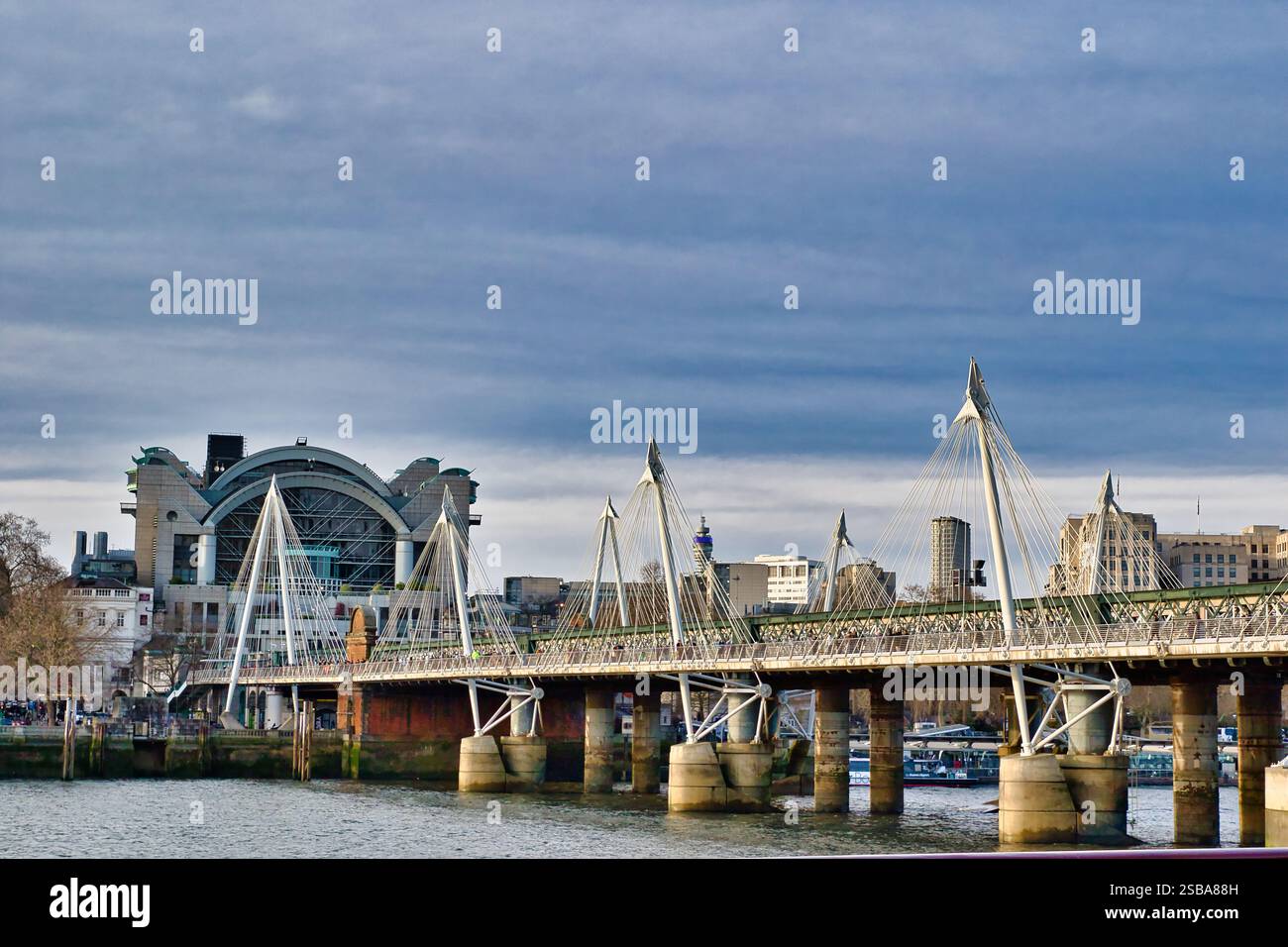 A cable-stayed pedestrian bridge spans a river, with a large modern ...