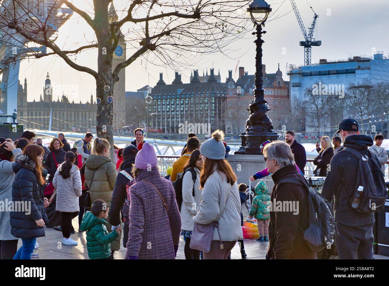 A crowd of people, many wearing winter clothing, gather outdoors near a ...