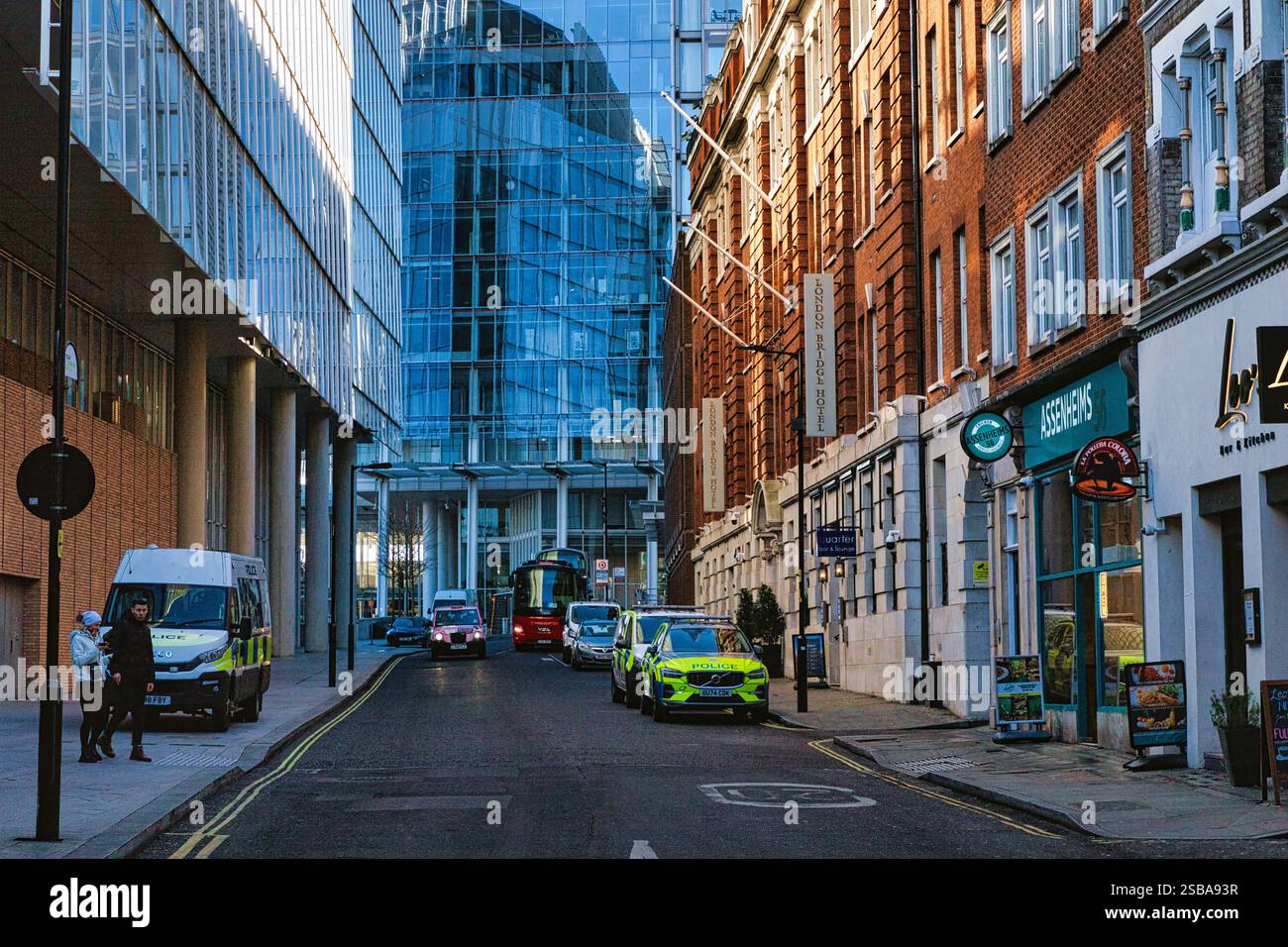 A city street scene shows two police cars parked, a police van, and ...