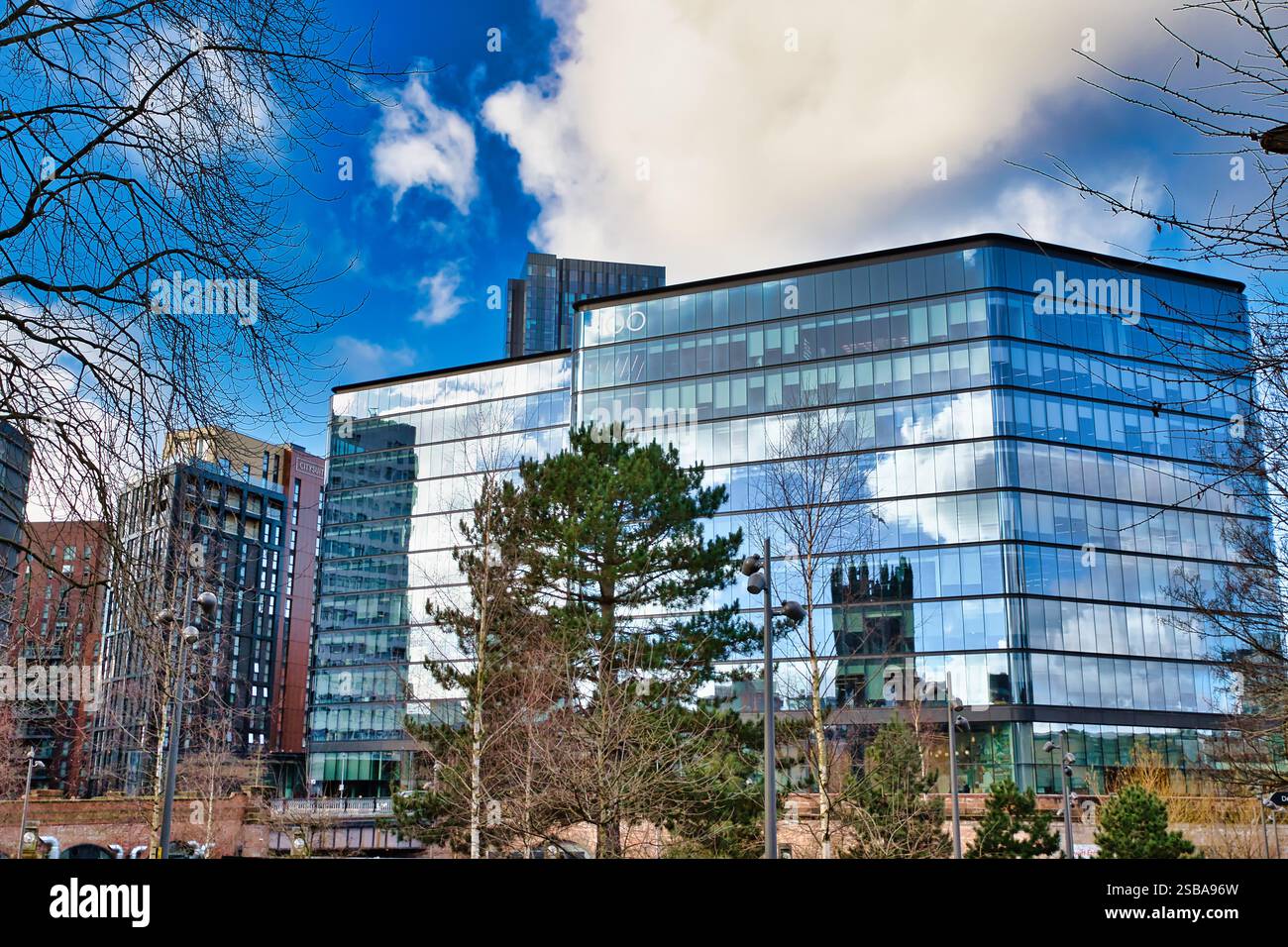 A modern glass-fronted building reflects a cloudy sky and surrounding ...