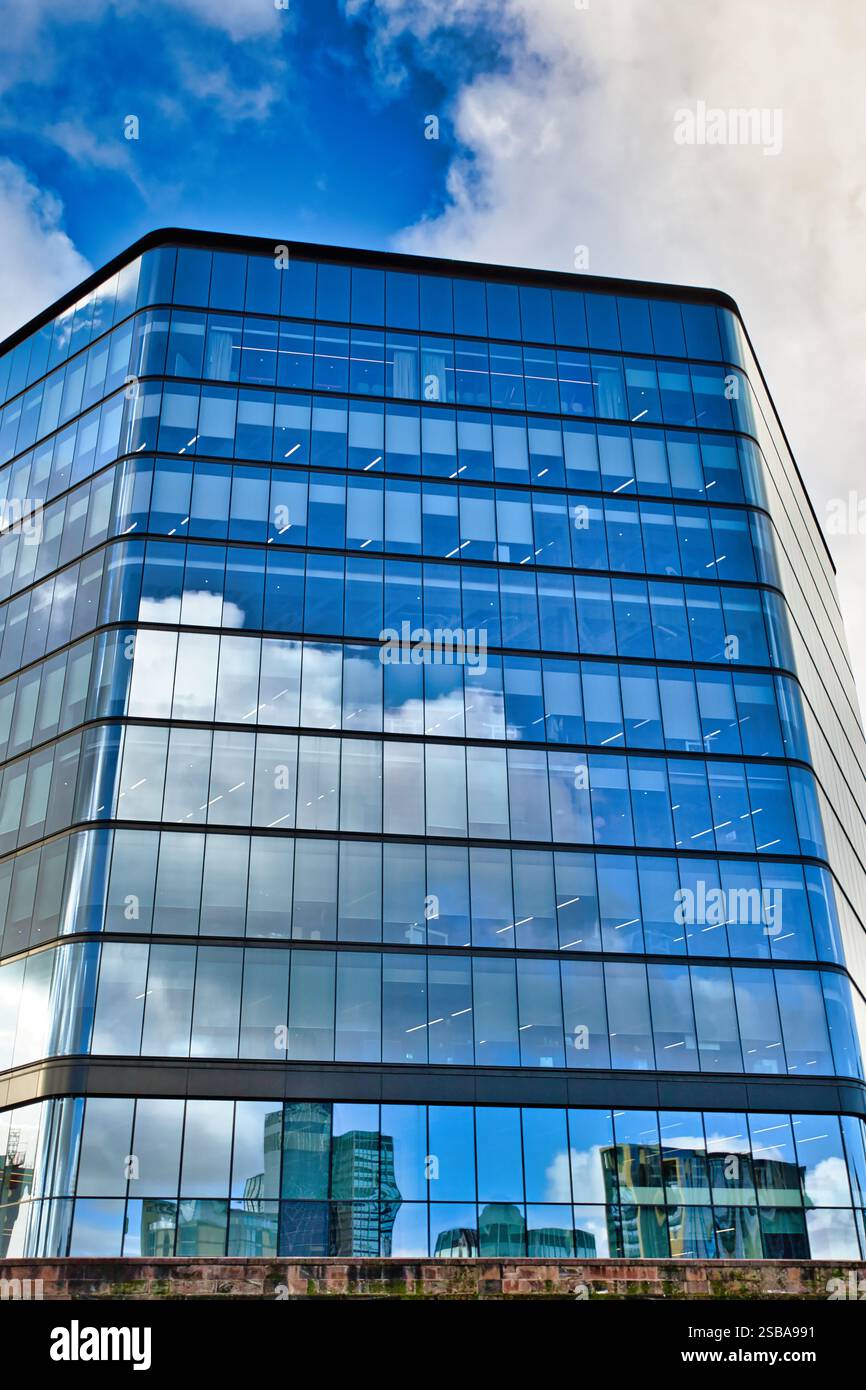 Modern glass skyscraper reflecting clouds and other buildings ...