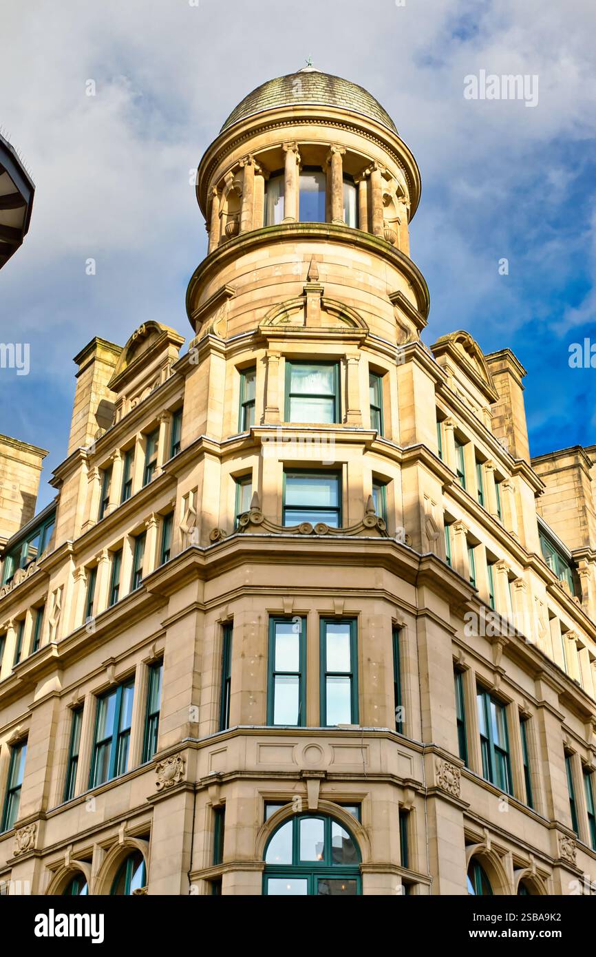 A tan-colored stone building with a prominent corner turret capped by a ...