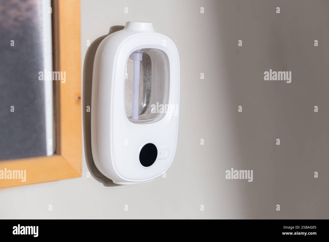 A white automatic hand sanitizer dispenser mounted on a wall next to a ...