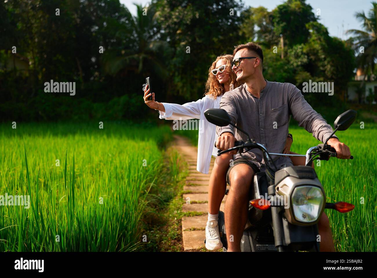 Couple on motorbike take selfie on rice field path. Man, woman on ...