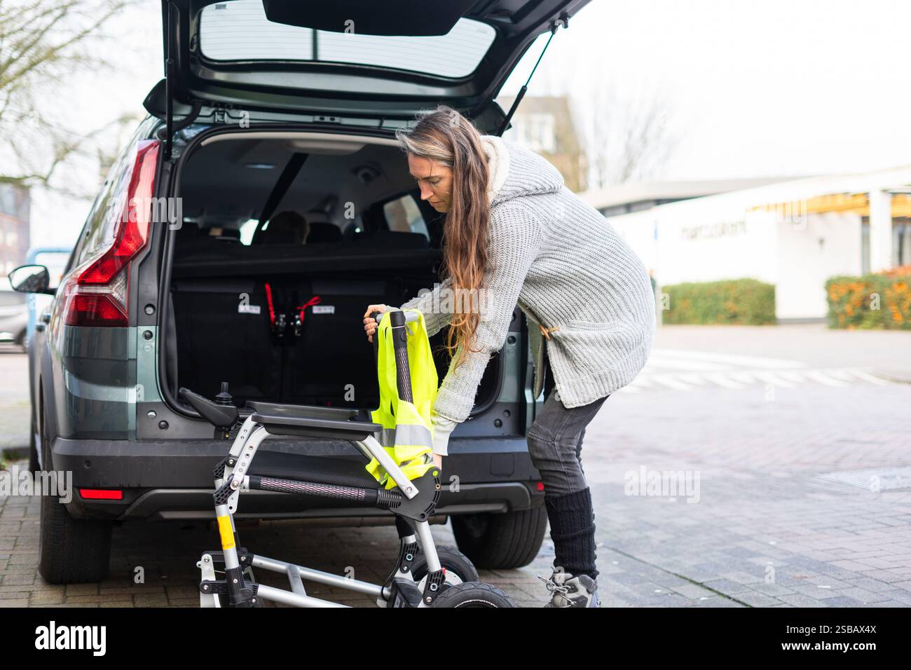 Woman taking folding electric wheelchair out of car trunk, preparing ...
