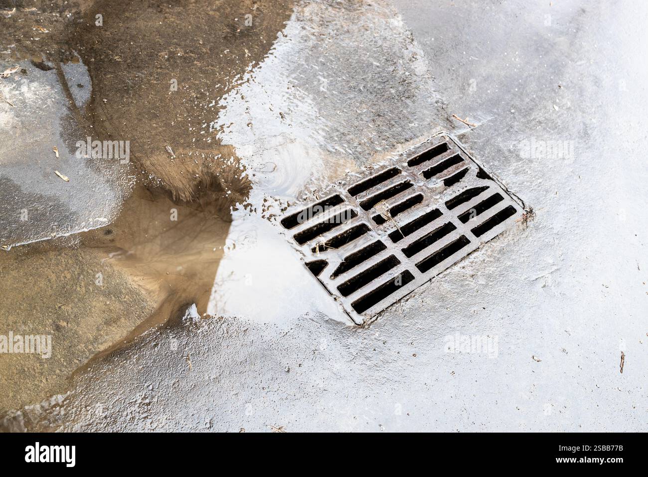 wet cast iron grate of street sewer and puddle on surface of city road ...