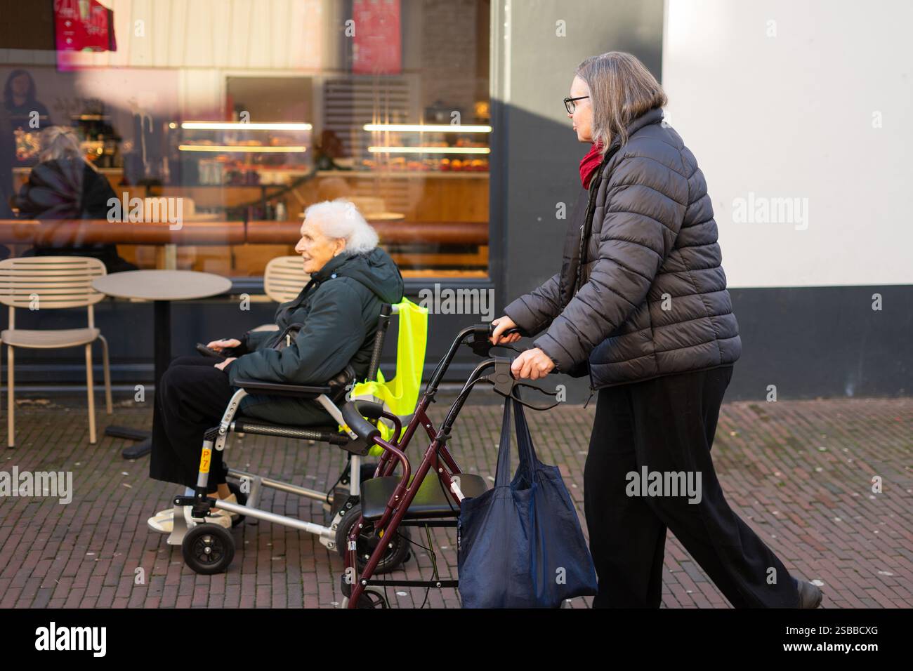 Mature woman walking with a walker next to elderly woman in wheelchair ...