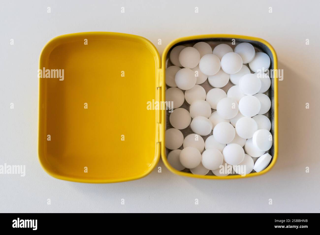 Yellow opened tin case full of white mints. White background ...