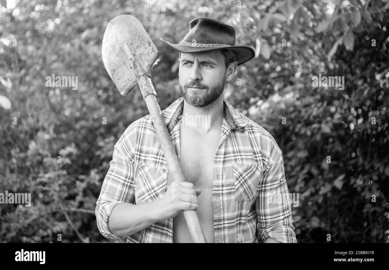 Serious man holding garden spade. Unshaven man wearing cowboy hat and ...